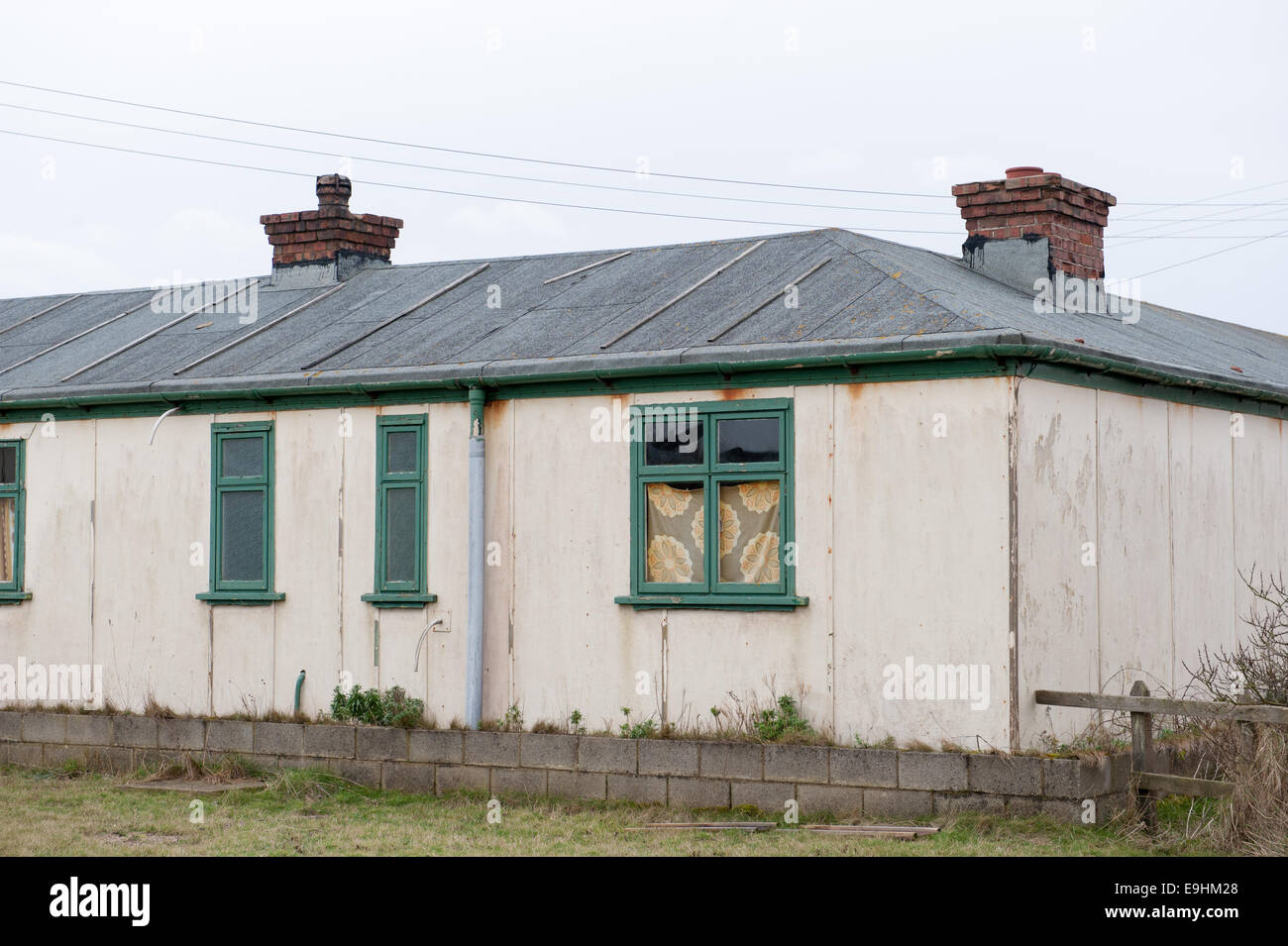 an old, weathered prefab bungalow with green window frames and curtains ...