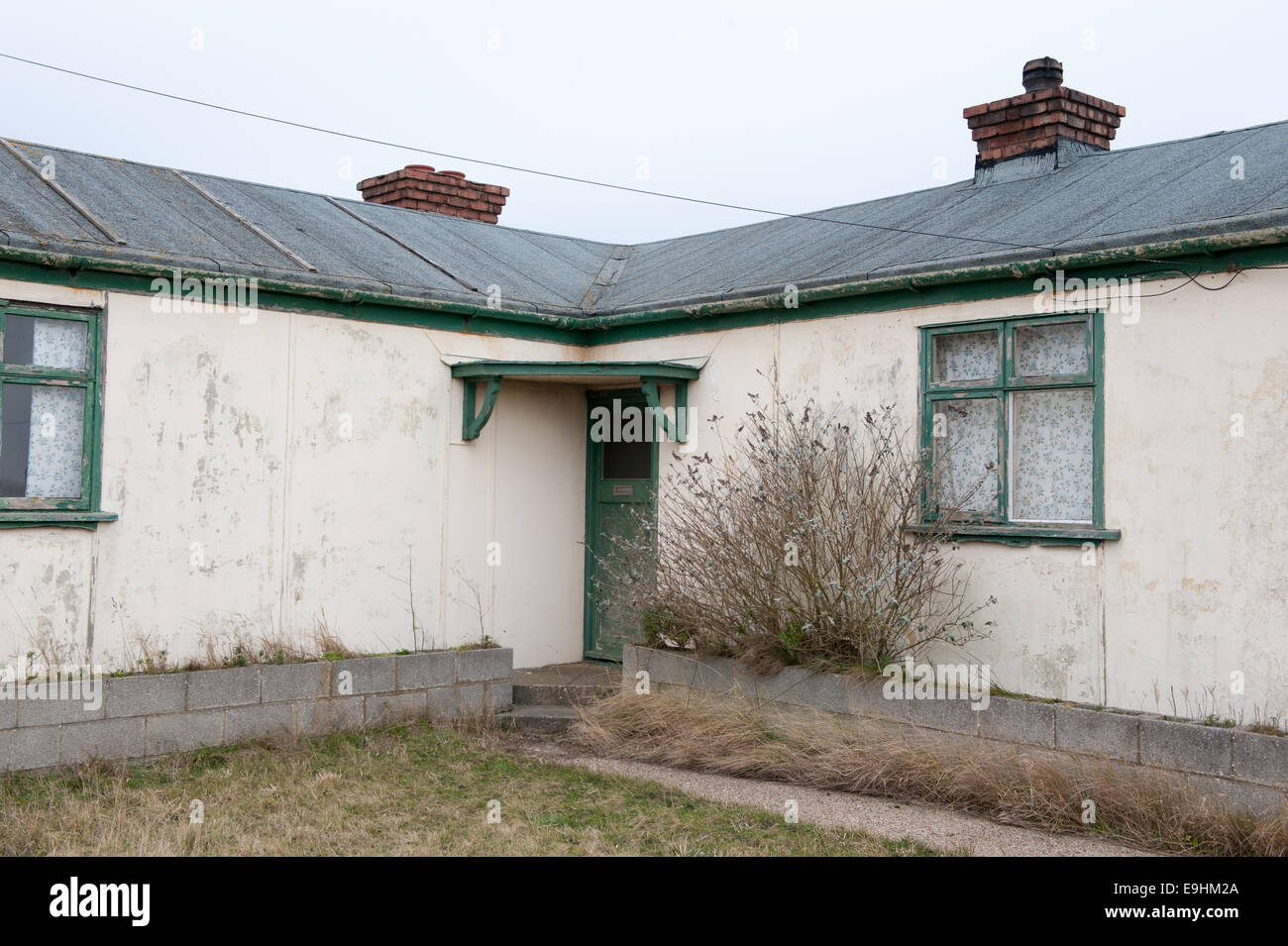 an old, weathered prefab bungalow with green window frames and curtains ...
