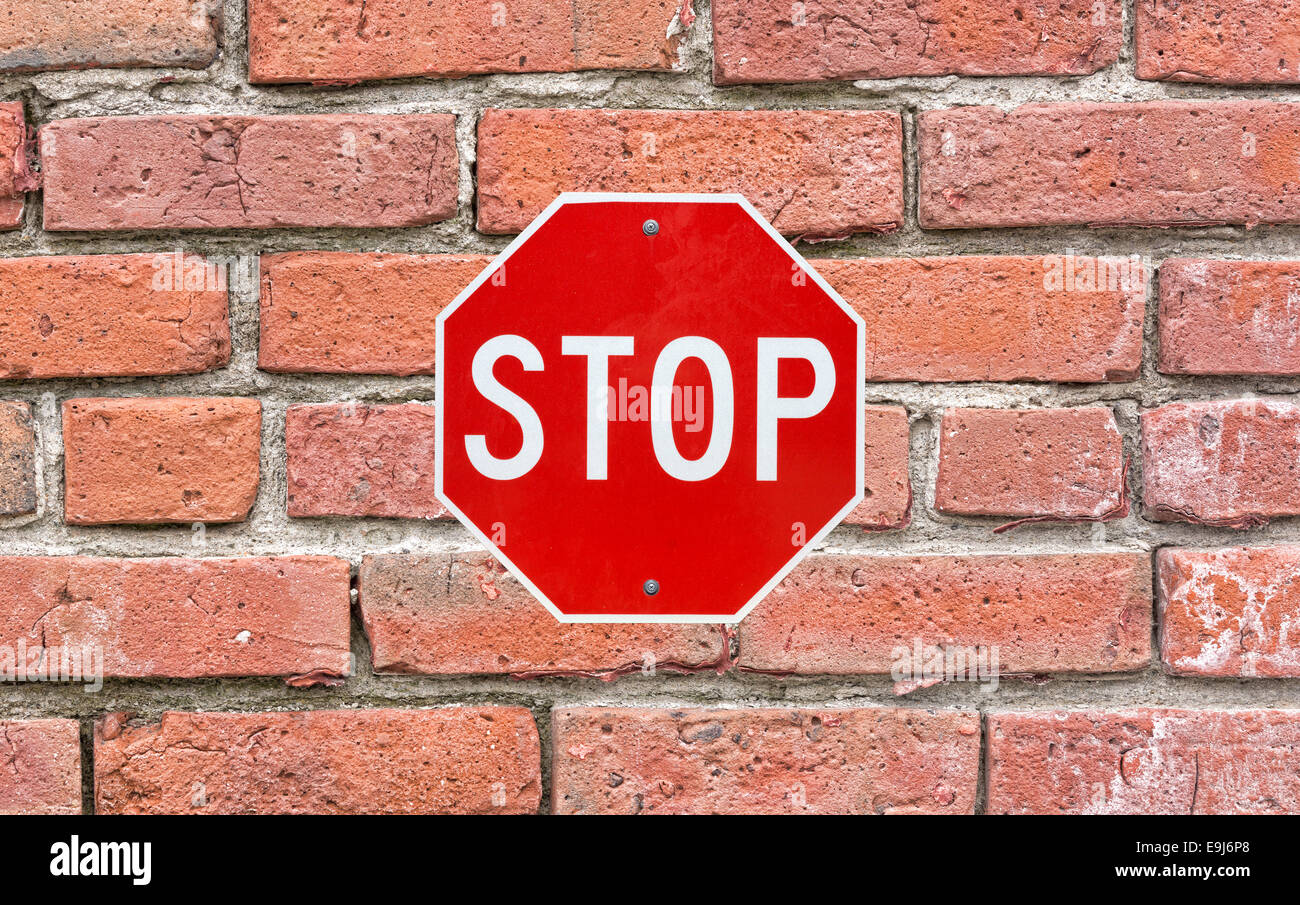 A bright red and white stop sign securely attached to a large old brick ...