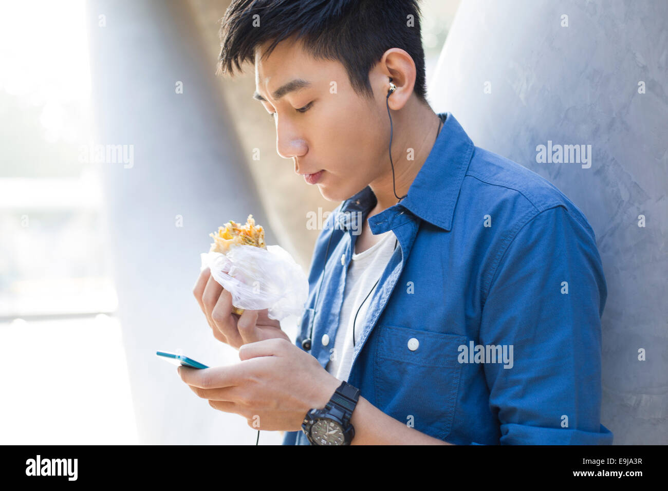 Young man listening to earphones and eating food Stock Photo - Alamy