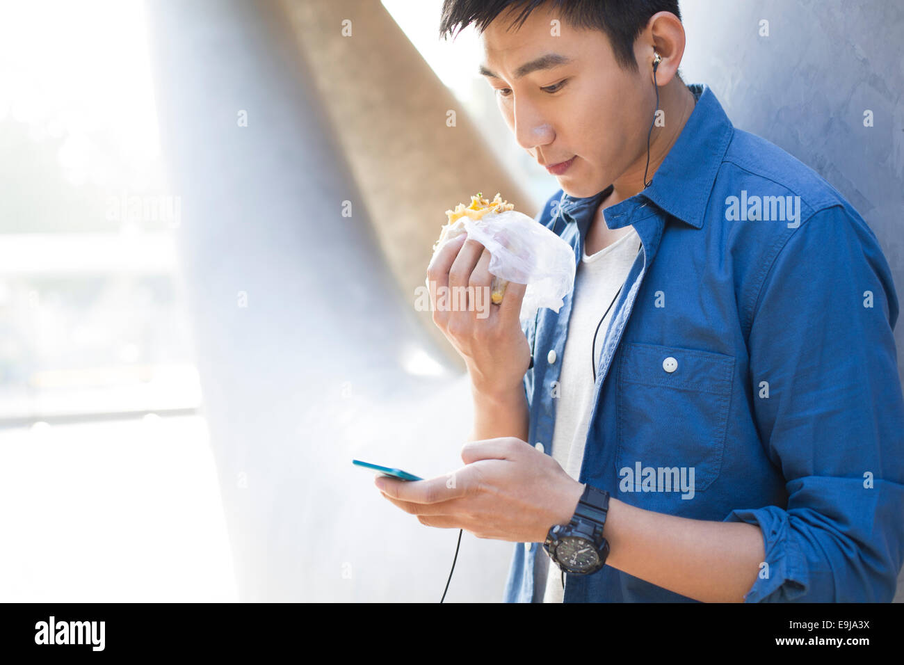 Young man listening to earphones and eating food Stock Photo - Alamy