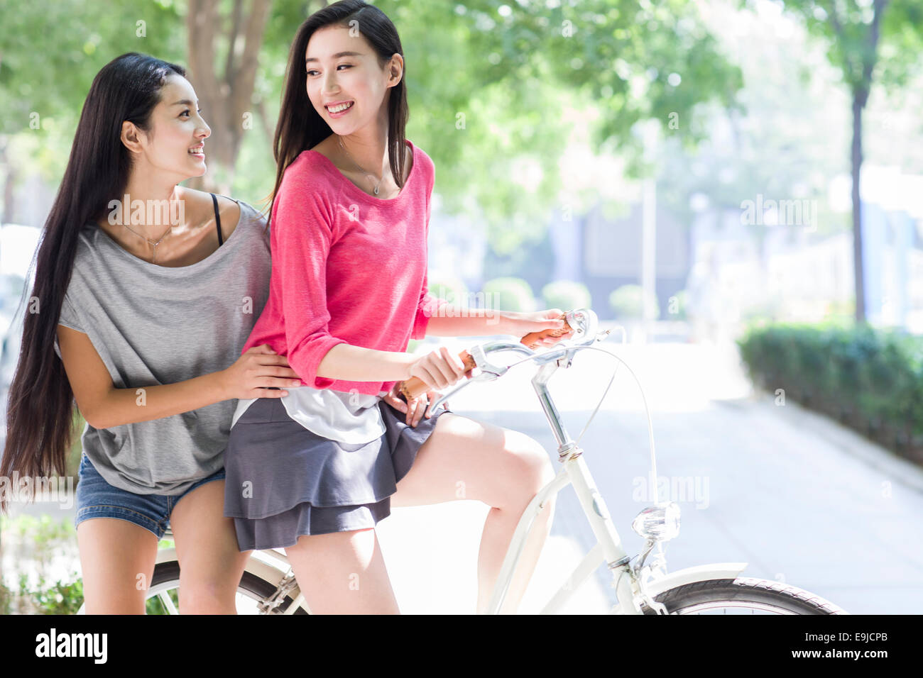 Best female friends riding bicycle at campus Stock Photo - Alamy
