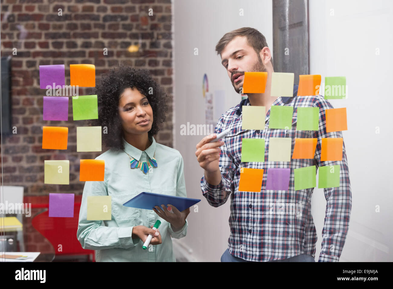 Team using digital tablet by sticky notes on window Stock Photo - Alamy
