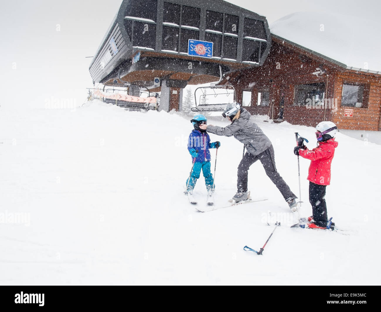 young family preparing to go skiing in front of a ski lift in heavy ...