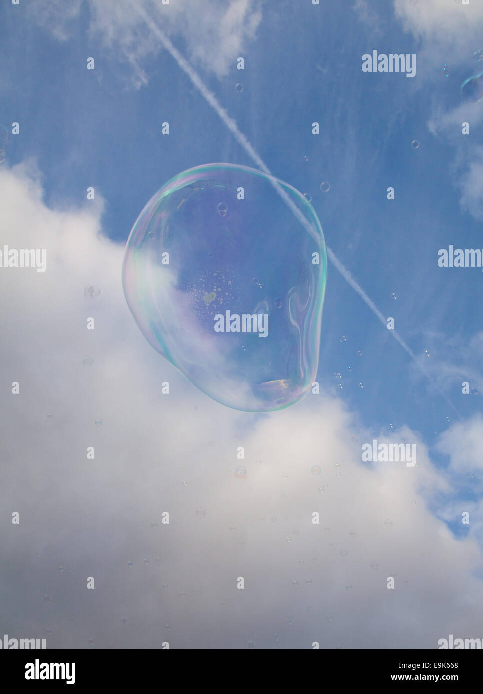 Giant bubble floating off into a blue cloudy sky with other smaller ...