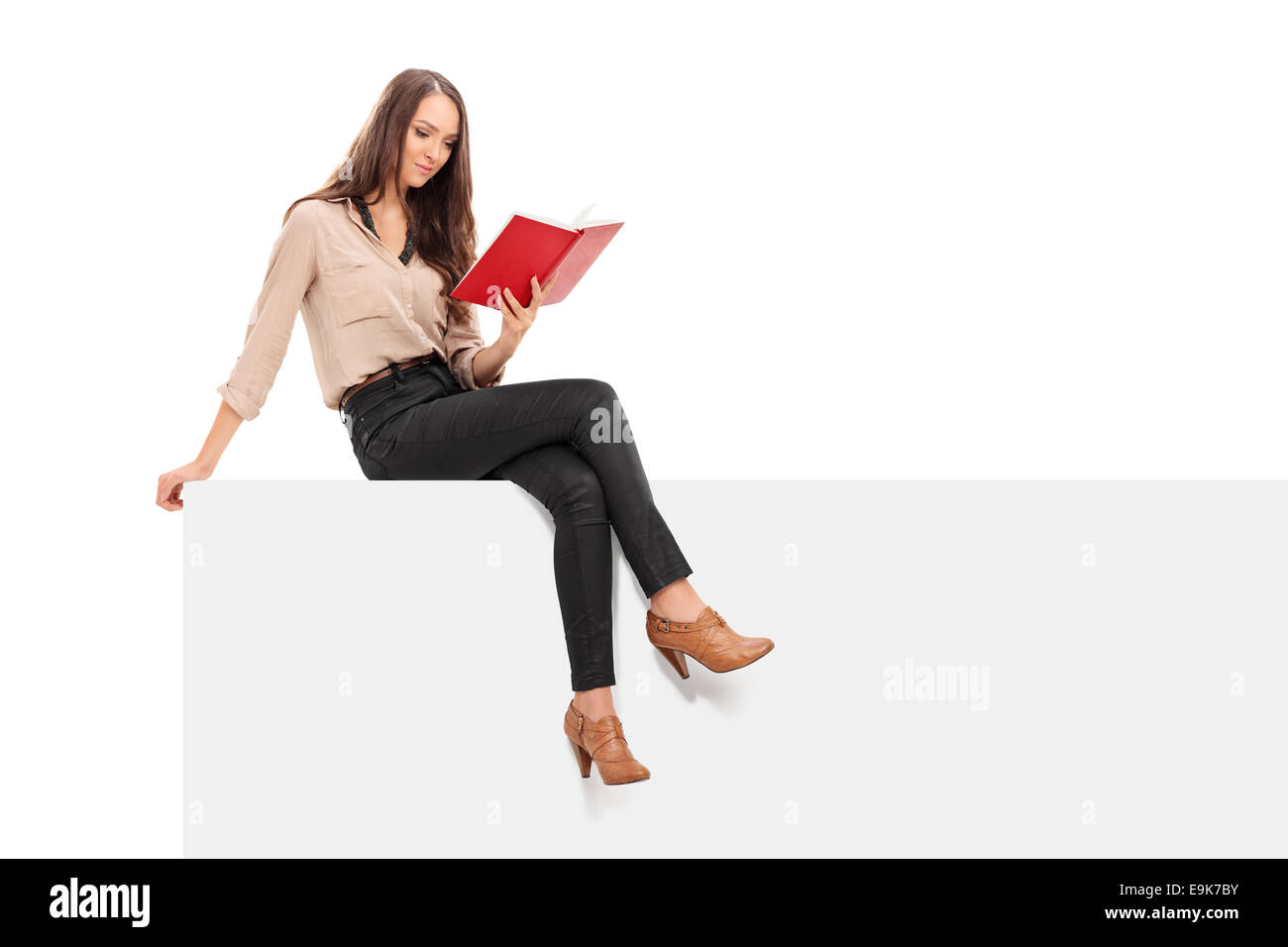 Young woman reading a book seated on a panel isolated on white ...