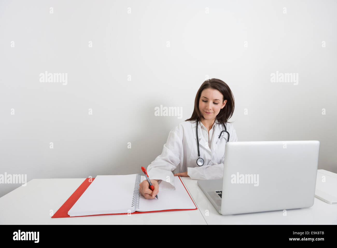 Female doctor writing on binder at desk in clinic Stock Photo - Alamy