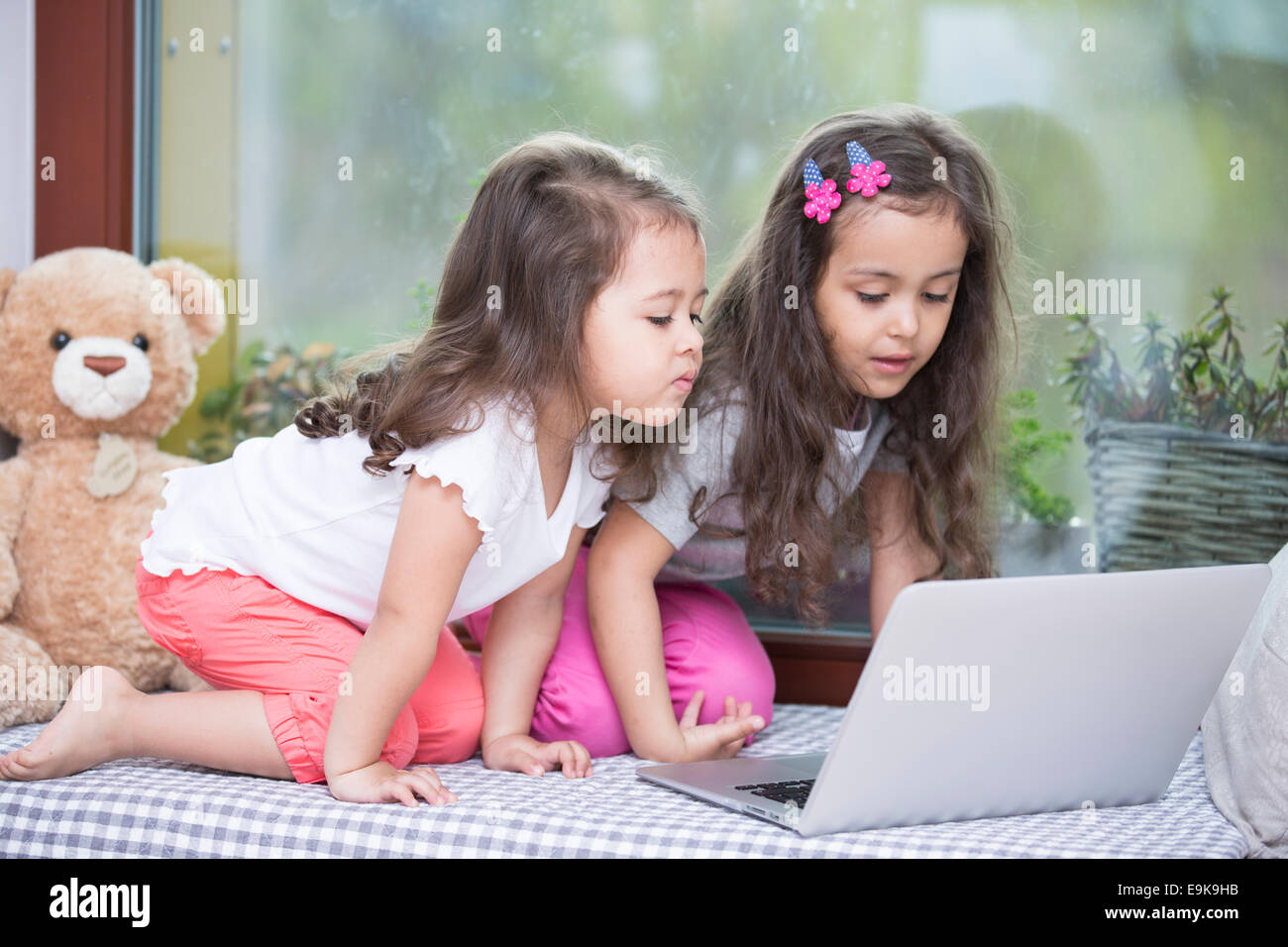 Cute little sisters using laptop on bed at home Stock Photo - Alamy