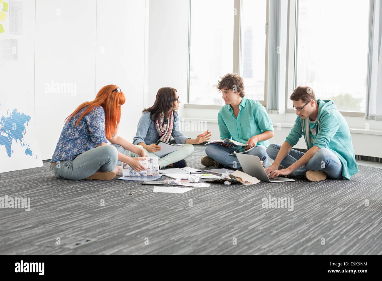 Creative businesspeople discussing while sitting on floor in office ...
