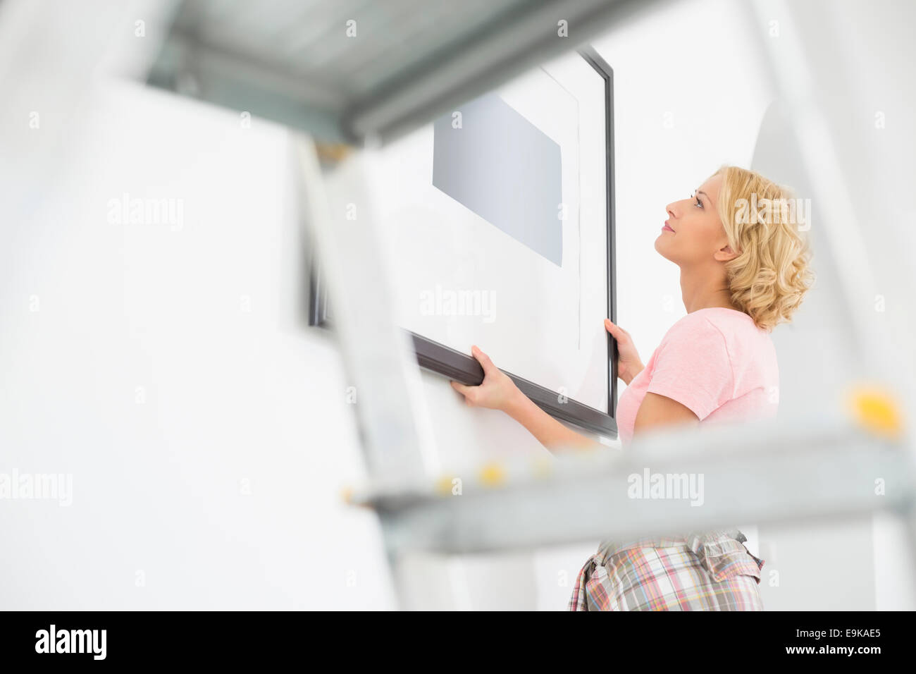 Woman positioning picture frame on wall Stock Photo - Alamy