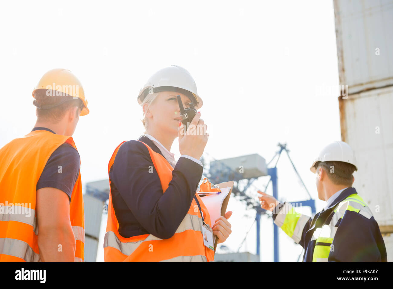 Female supervisor using walkie-talkie while workers discussing in ...