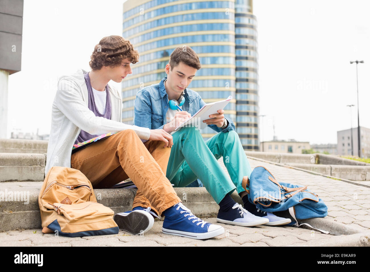 Full length of young male college students studying on steps against ...