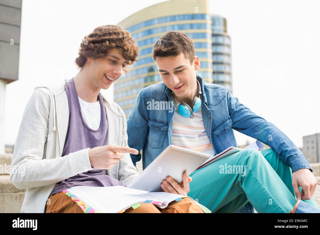 Happy young male college students using digital tablet against building ...