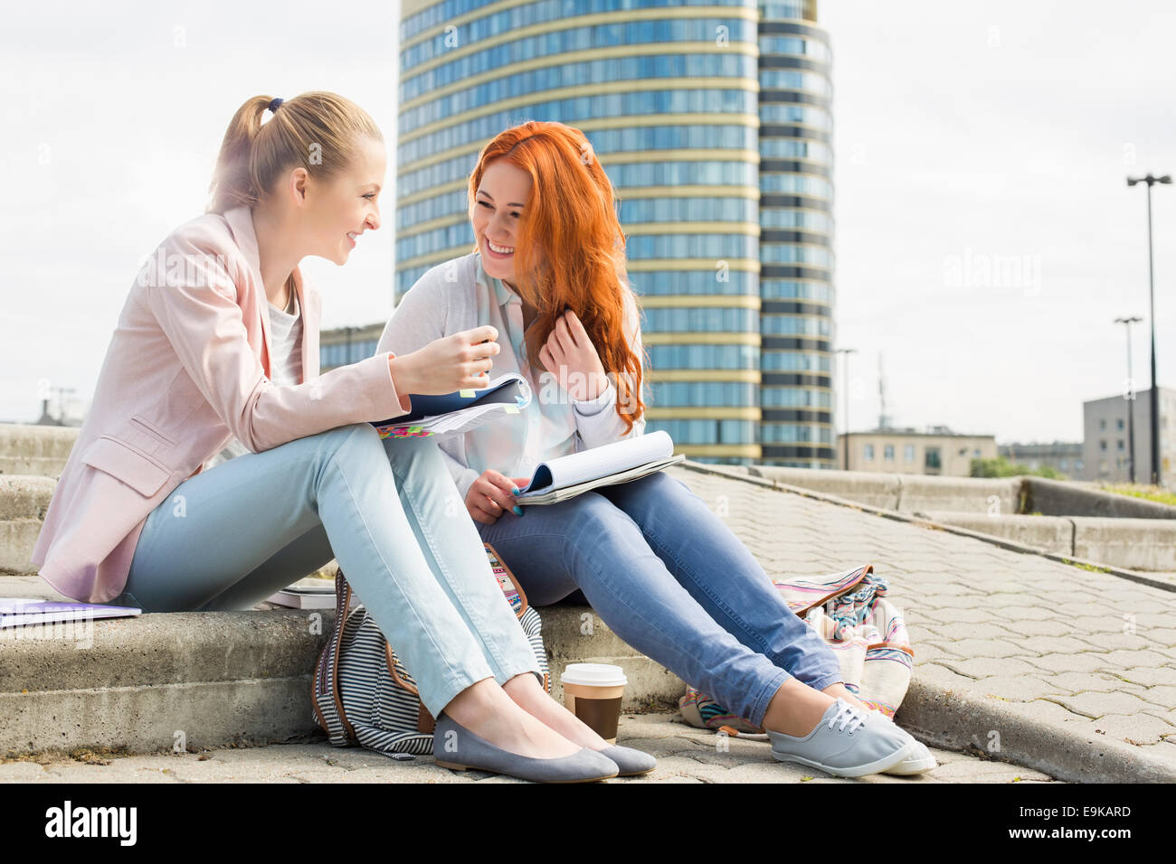 Full length of smiling female college students studying on steps ...