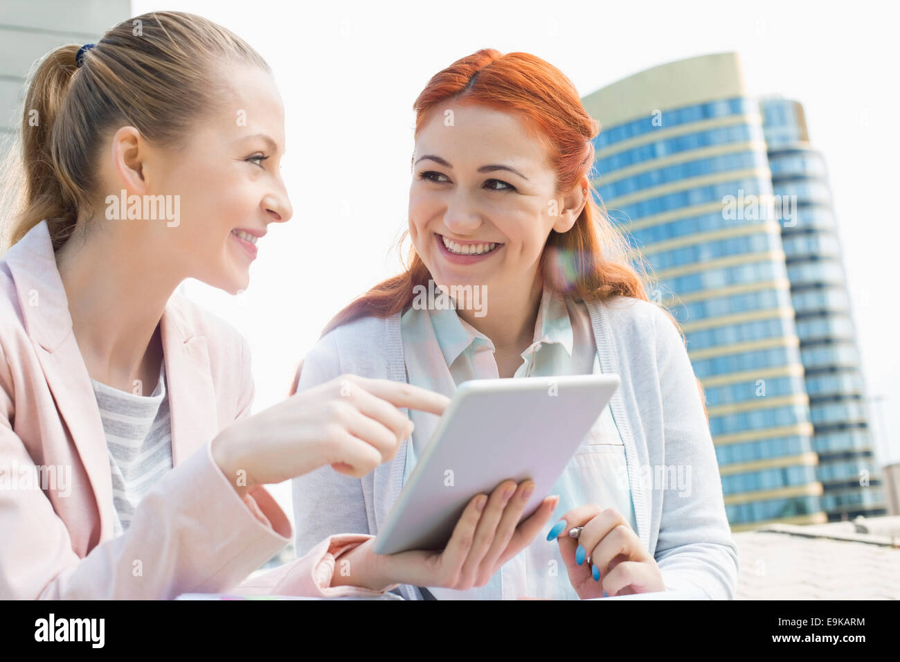 Smiling young university students using tablet PC against building ...