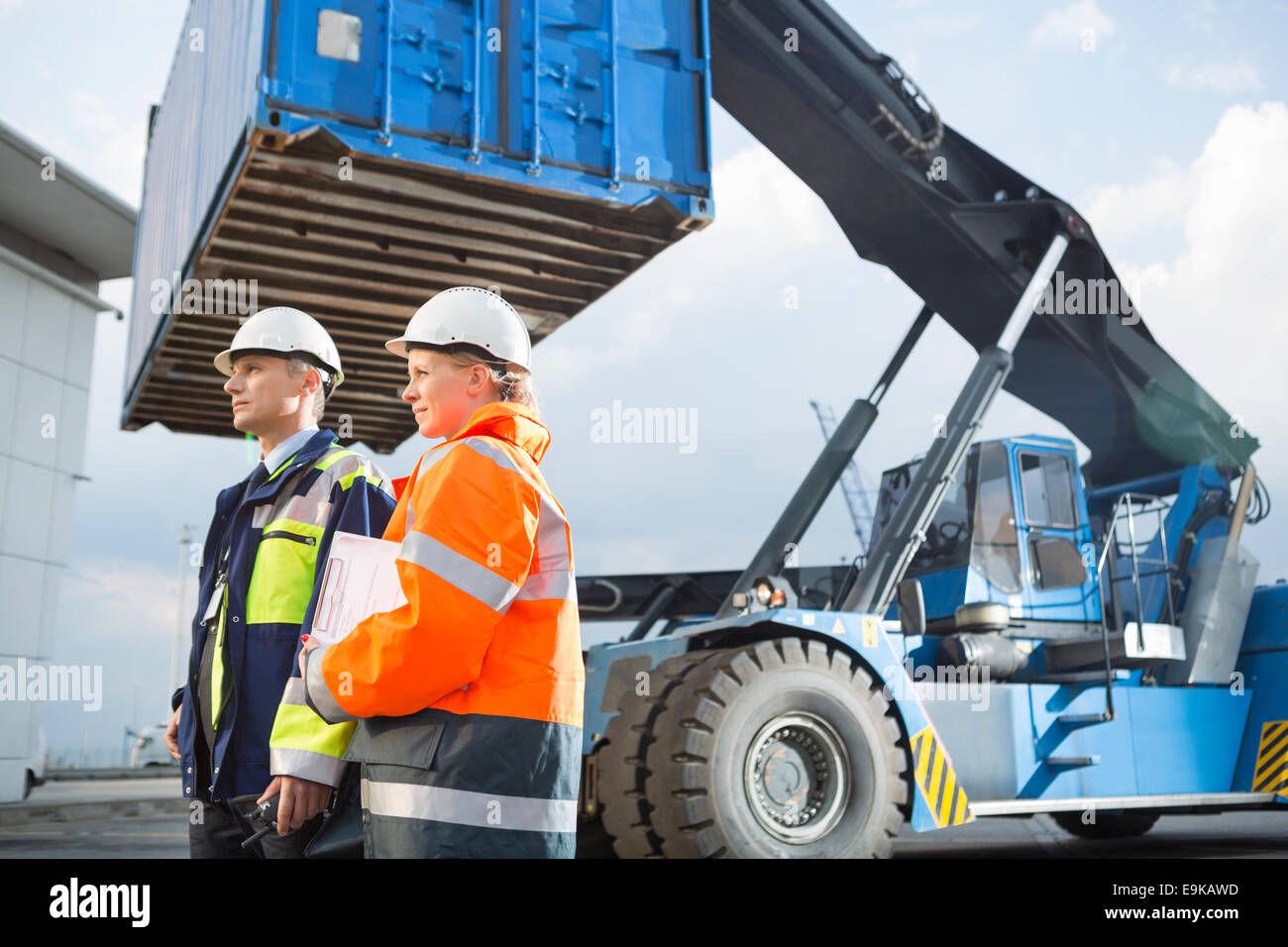 Male and female workers standing by freight vehicle in shipping yard ...