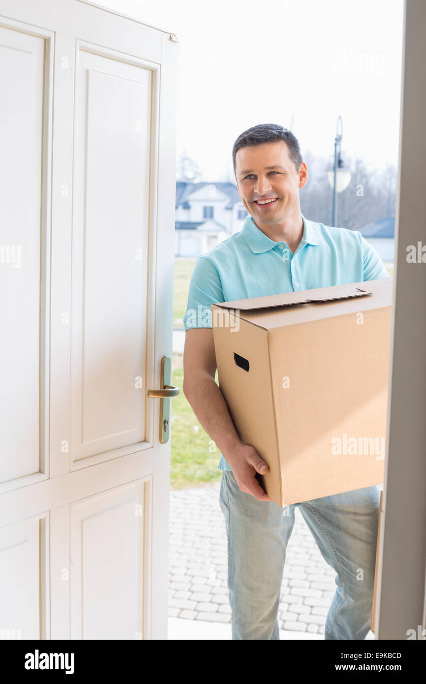 Happy man carrying cardboard box while entering new house Stock Photo ...