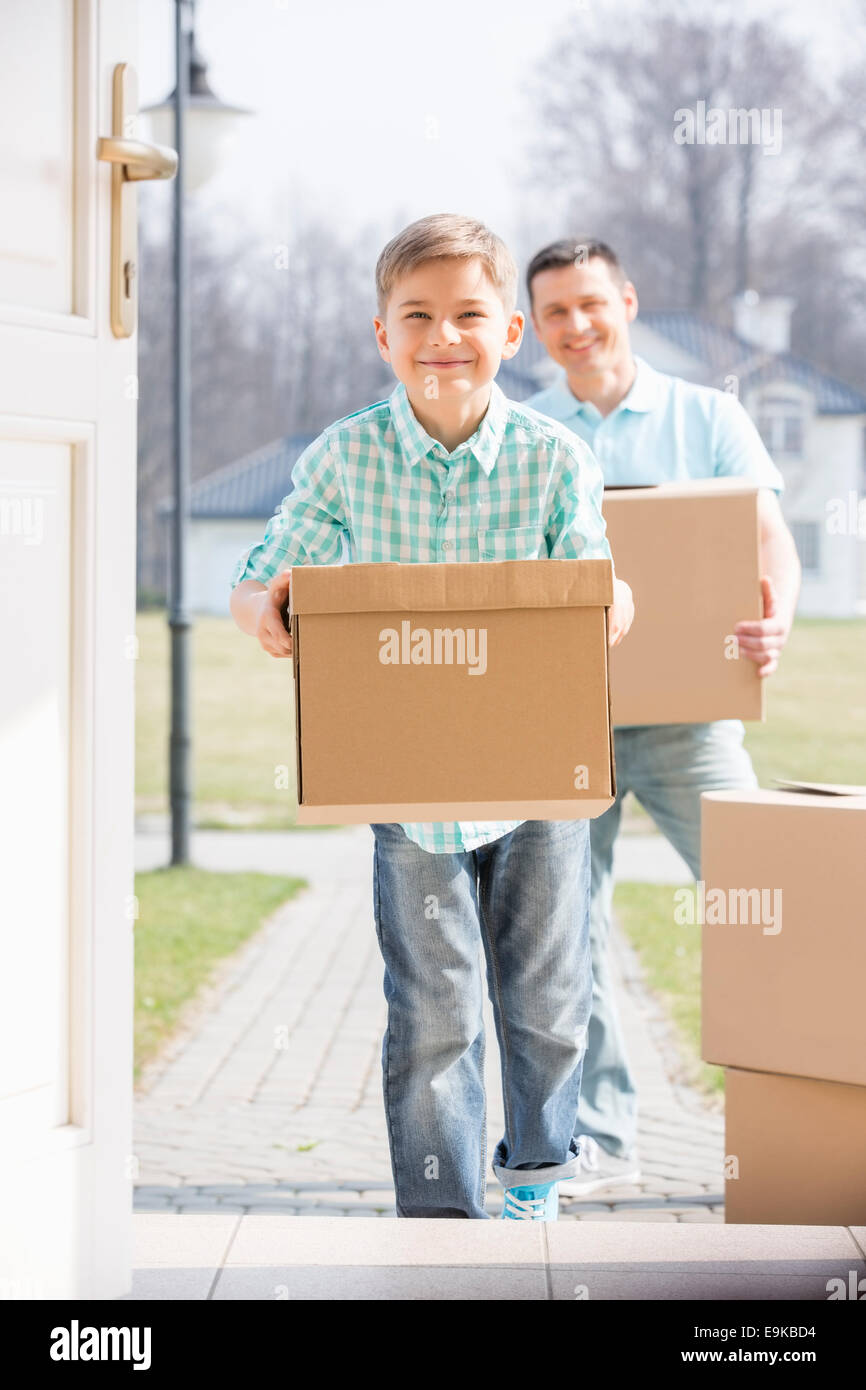 Happy father and son with cardboard boxes entering new home Stock Photo ...