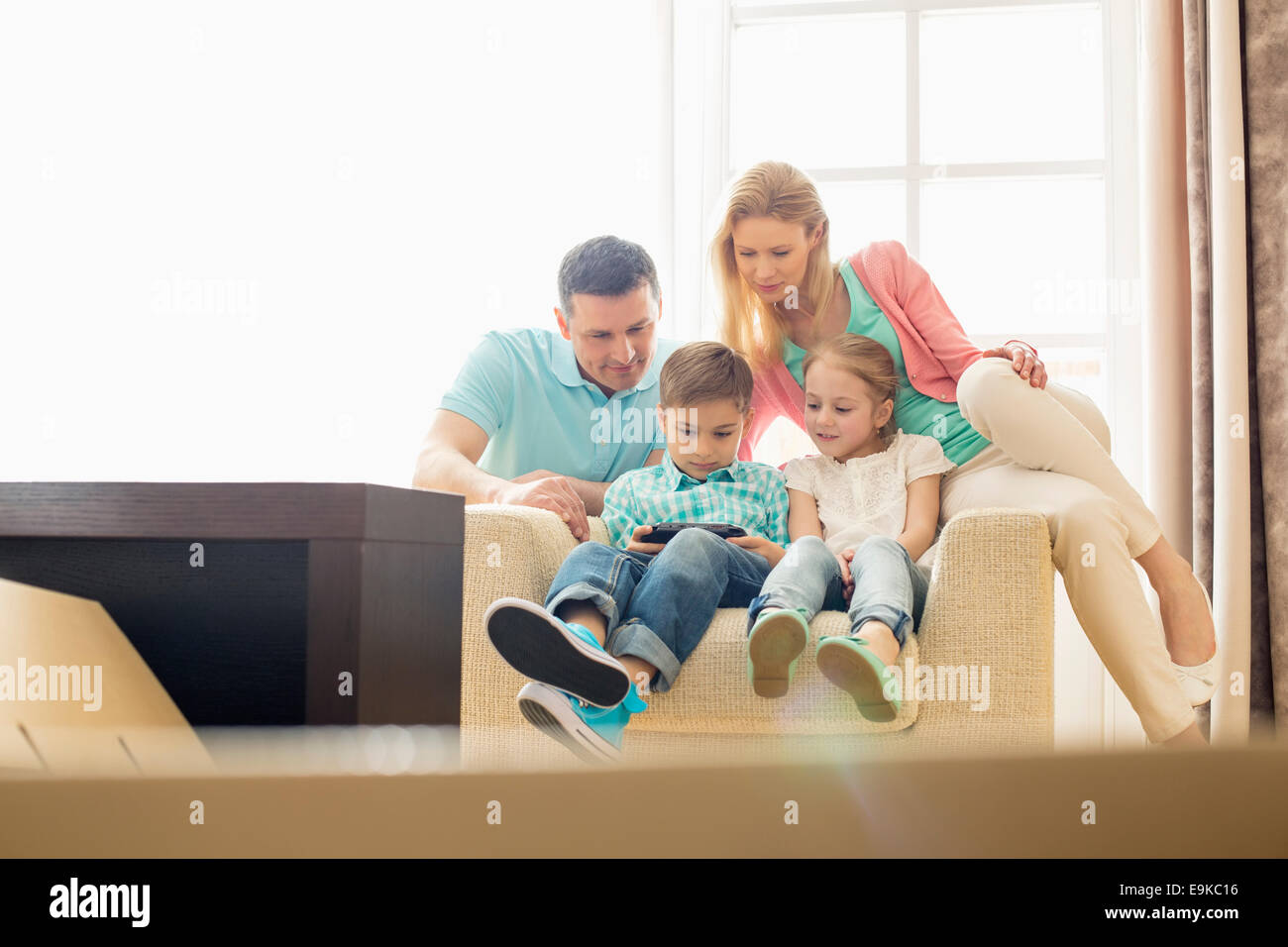 Family looking at boy playing hand-held video game at home Stock Photo ...