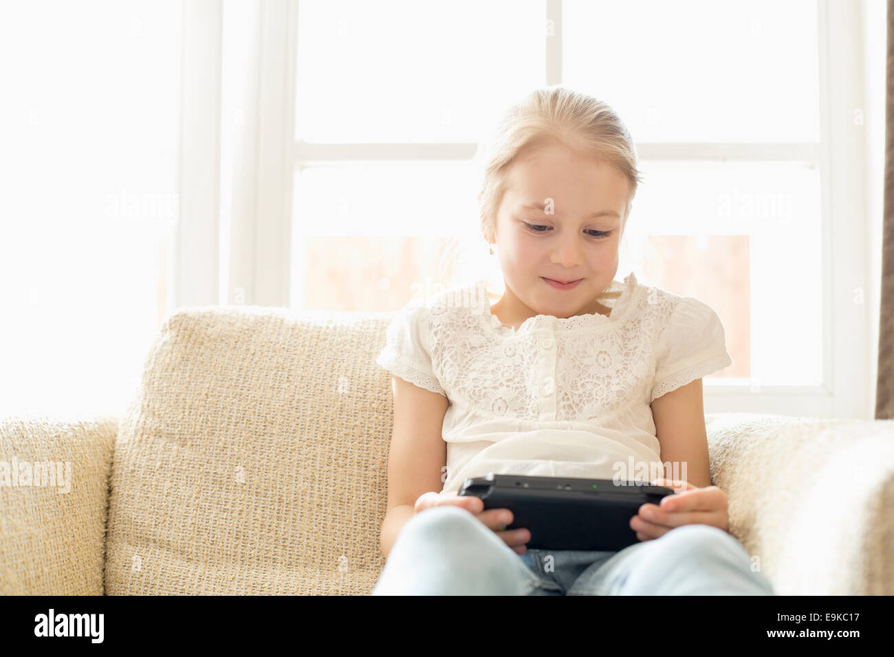 Cute girl playing hand-held video game at home Stock Photo - Alamy