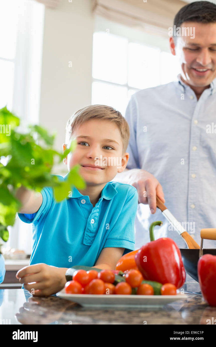Smiling boy touching houseplant with father preparing food in kitchen ...