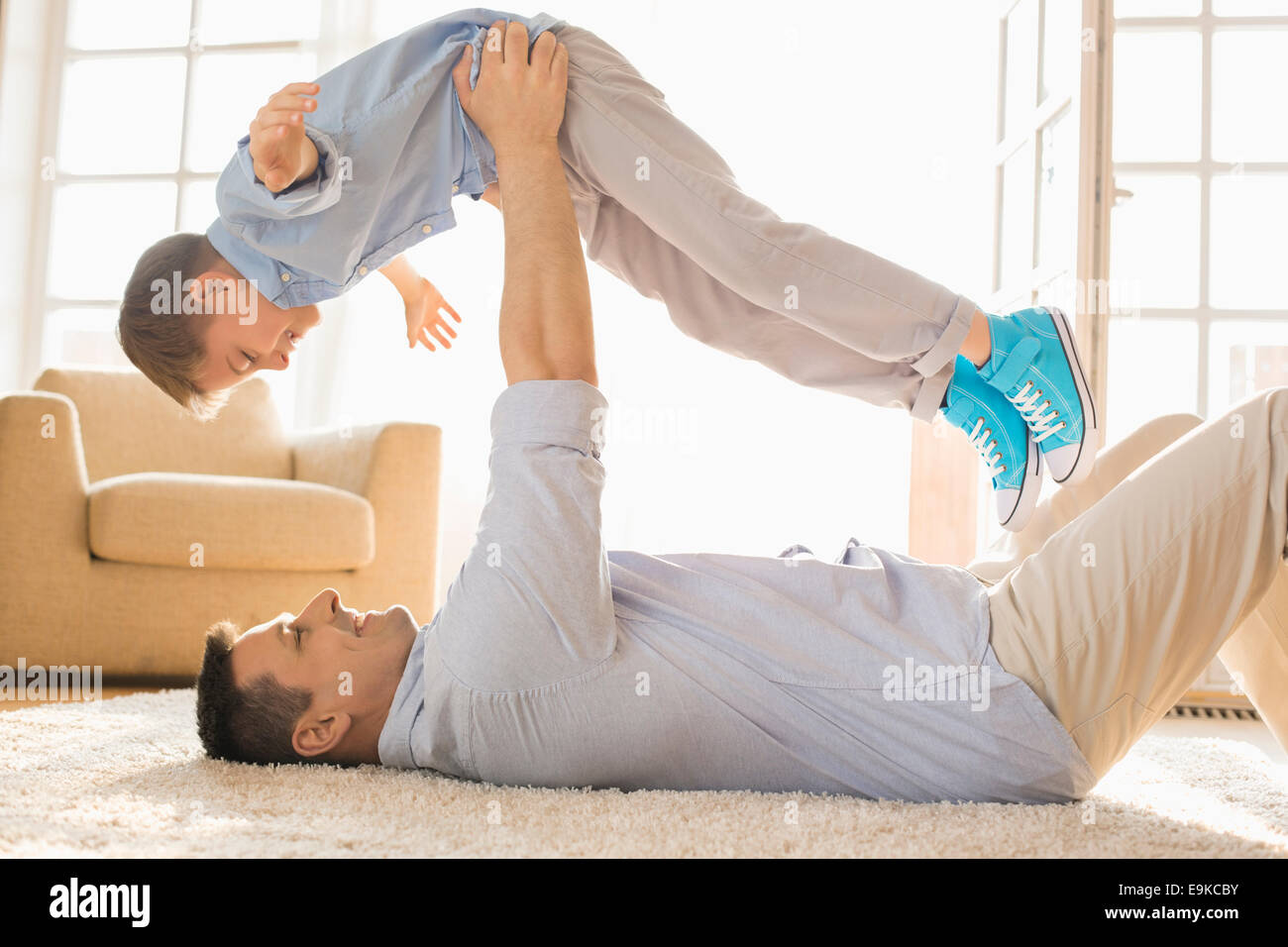 Side view of playful father lifting son while lying on floor at home ...