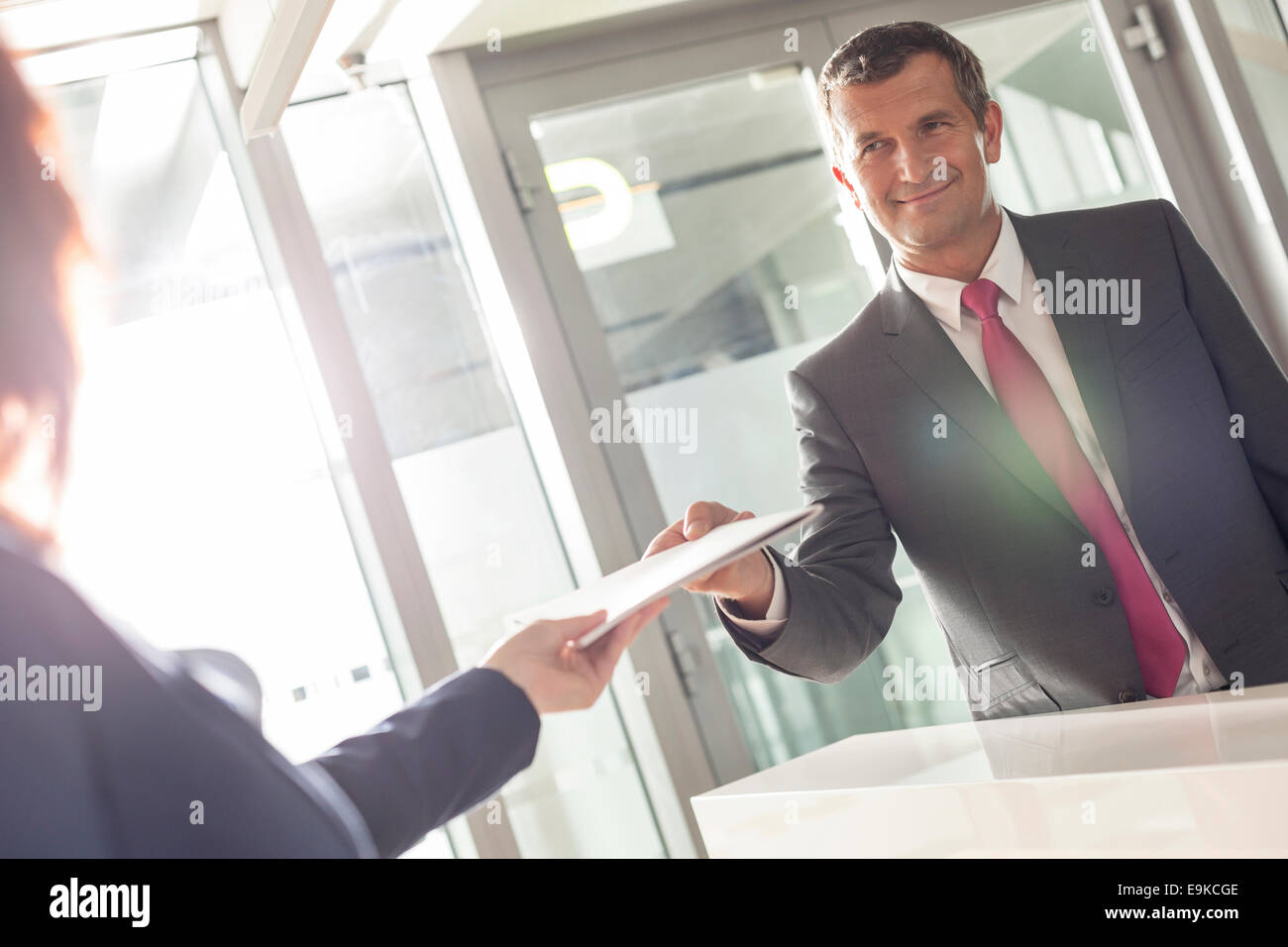 Businessman receiving document from receptionist in office Stock Photo ...