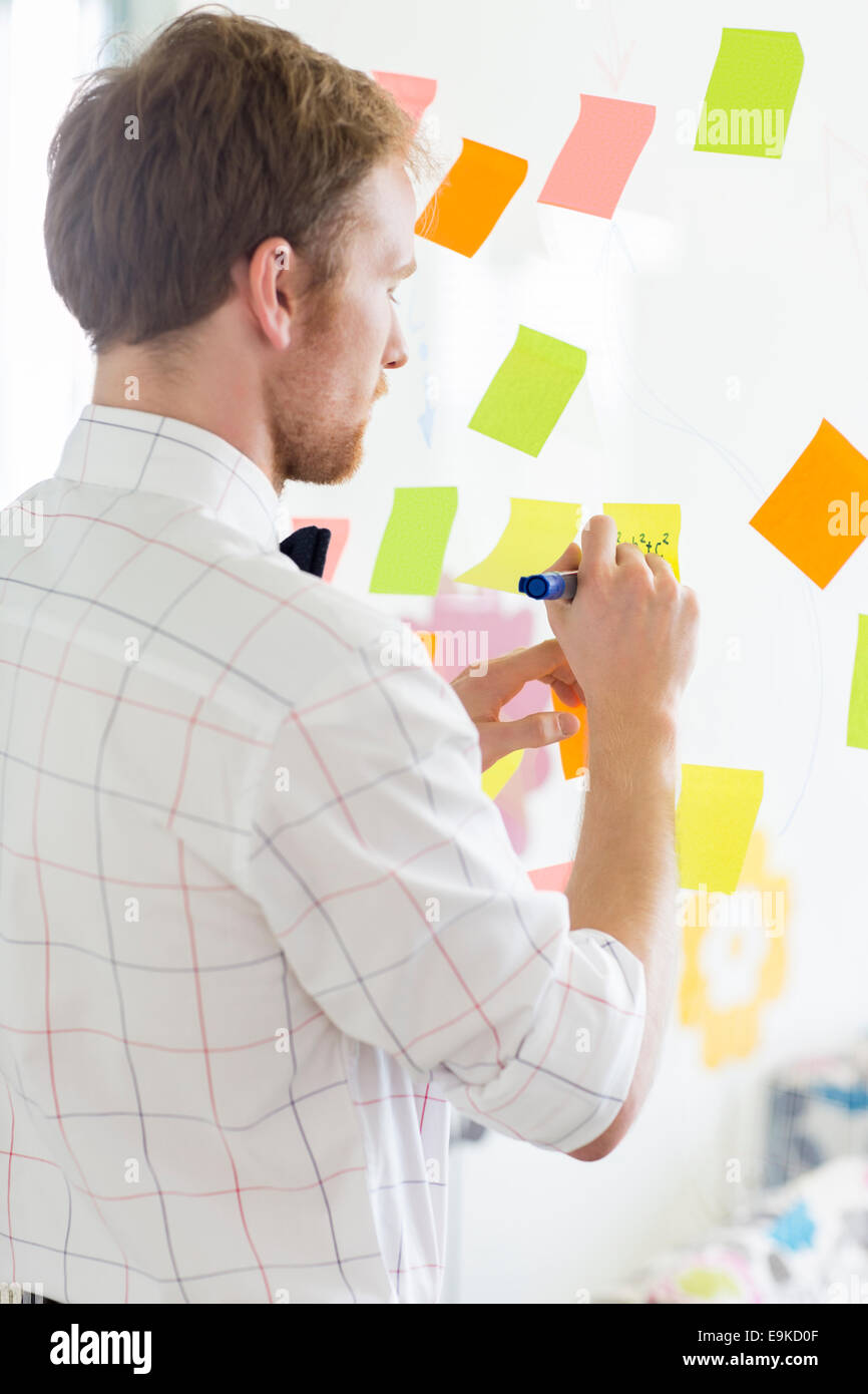 Rear view of businessman writing on sticky paper at creative office ...