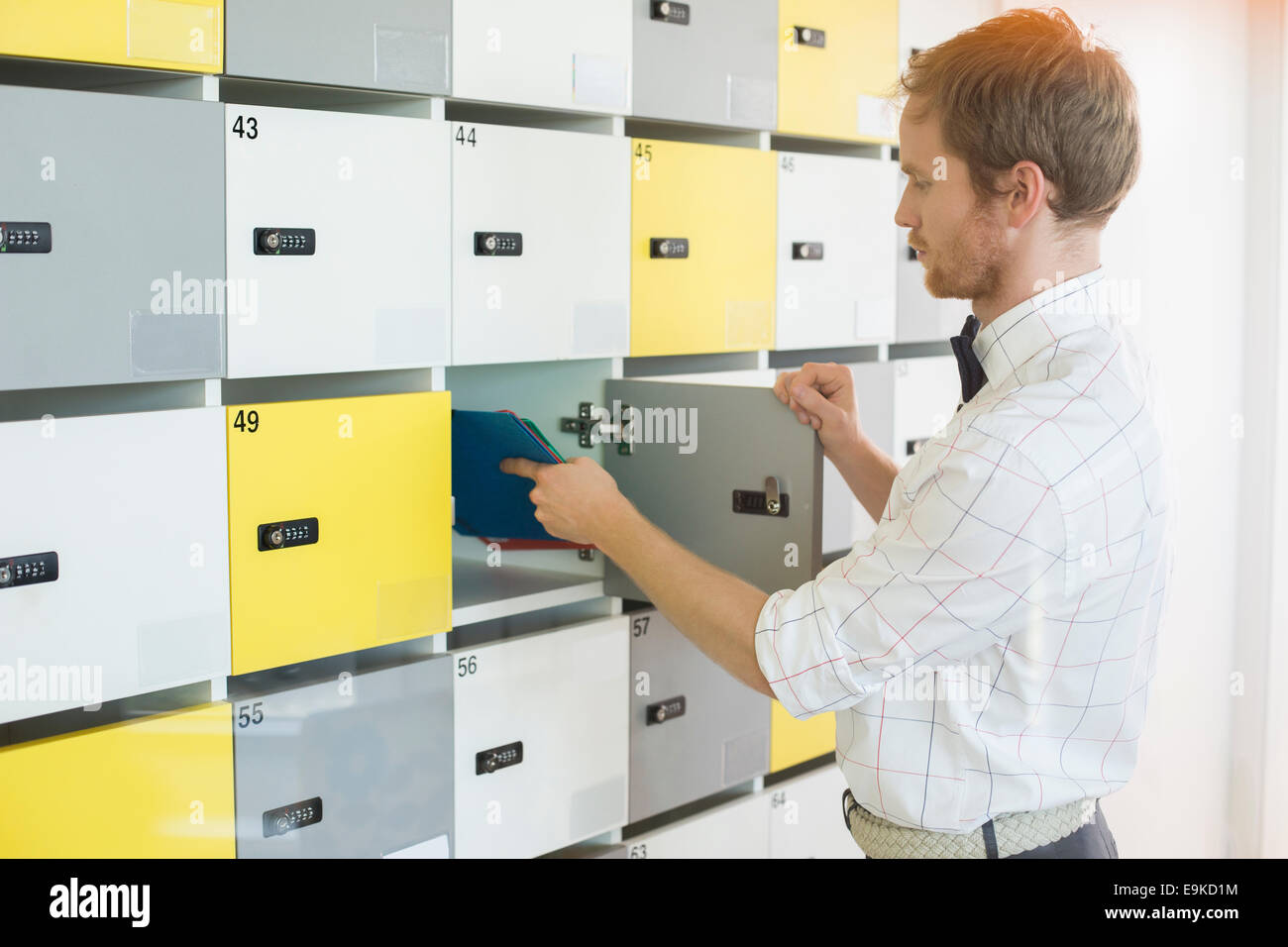 Side view of creative businessman putting files in locker at office ...