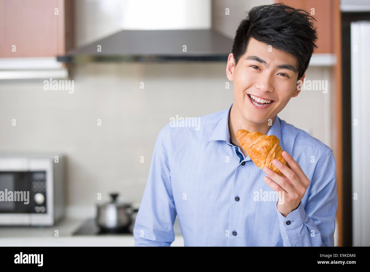 Happy young man eating bread in the kitchen Stock Photo - Alamy