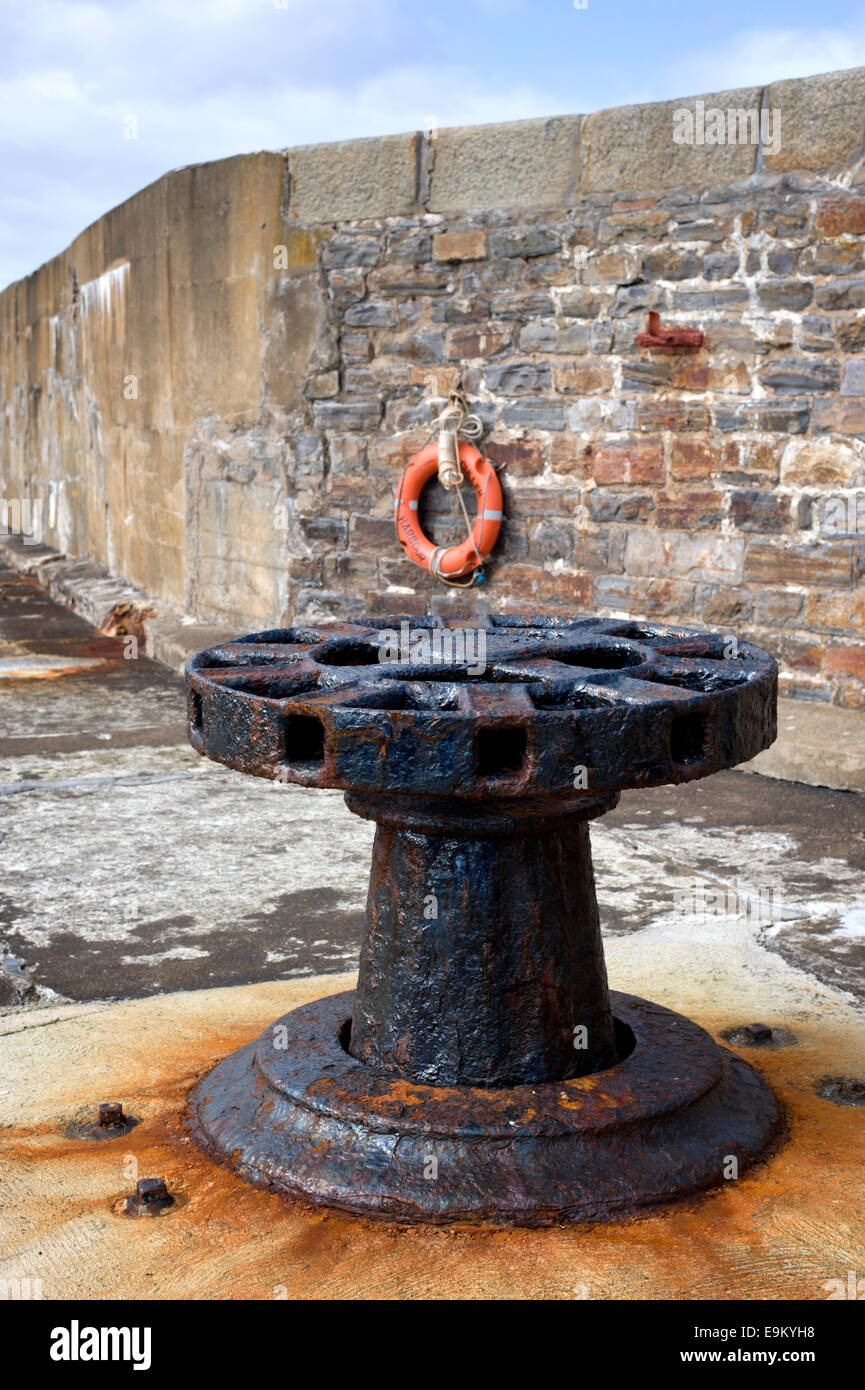 Rusty old harbourside capstan at Cullen with the main harbour wall in ...
