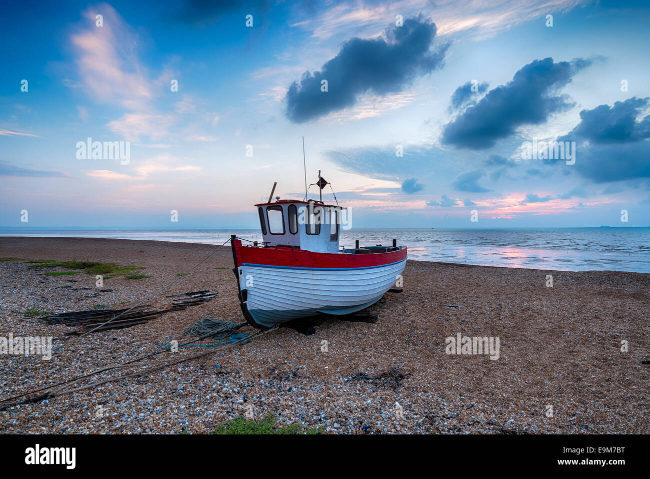 A small red and white fishing boat at sunrise on a pebble beach Stock ...