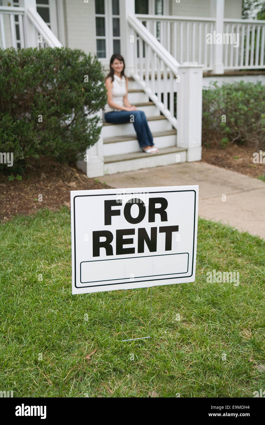 A young woman sitting on the steps of a house behind a ‘for rent’ sign ...