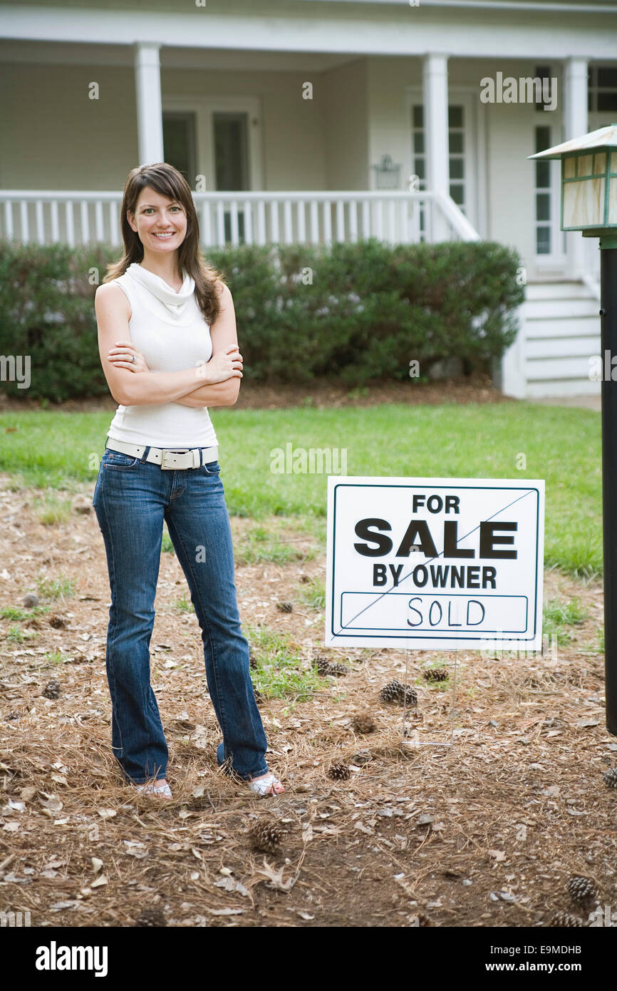 A young woman standing next to a ‘sold’ sign in front of a house Stock ...