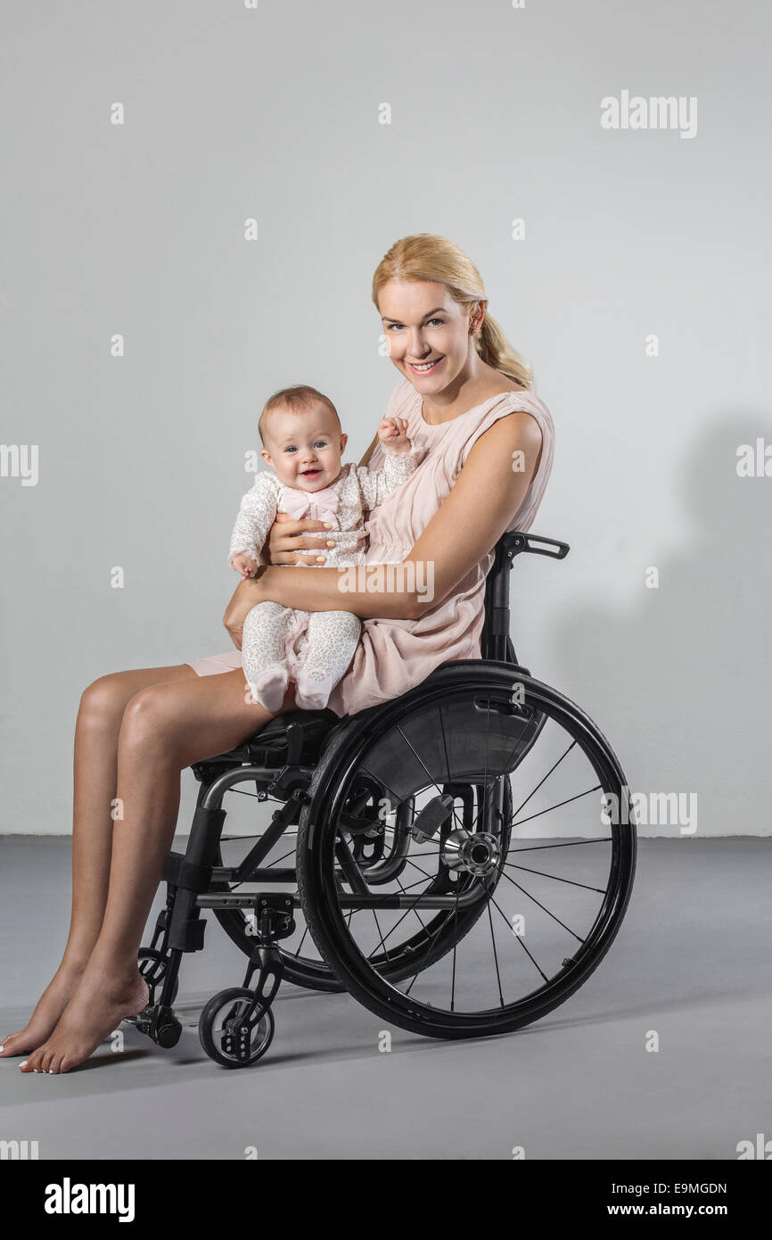 Full length portrait of happy woman with baby girl in wheelchair ...
