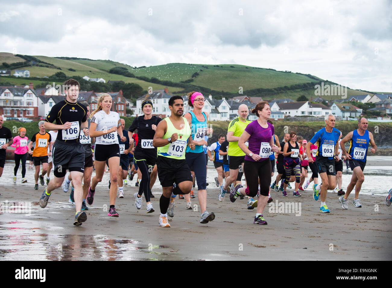 A mixed group of people competing running in a 10k race on the beach at ...