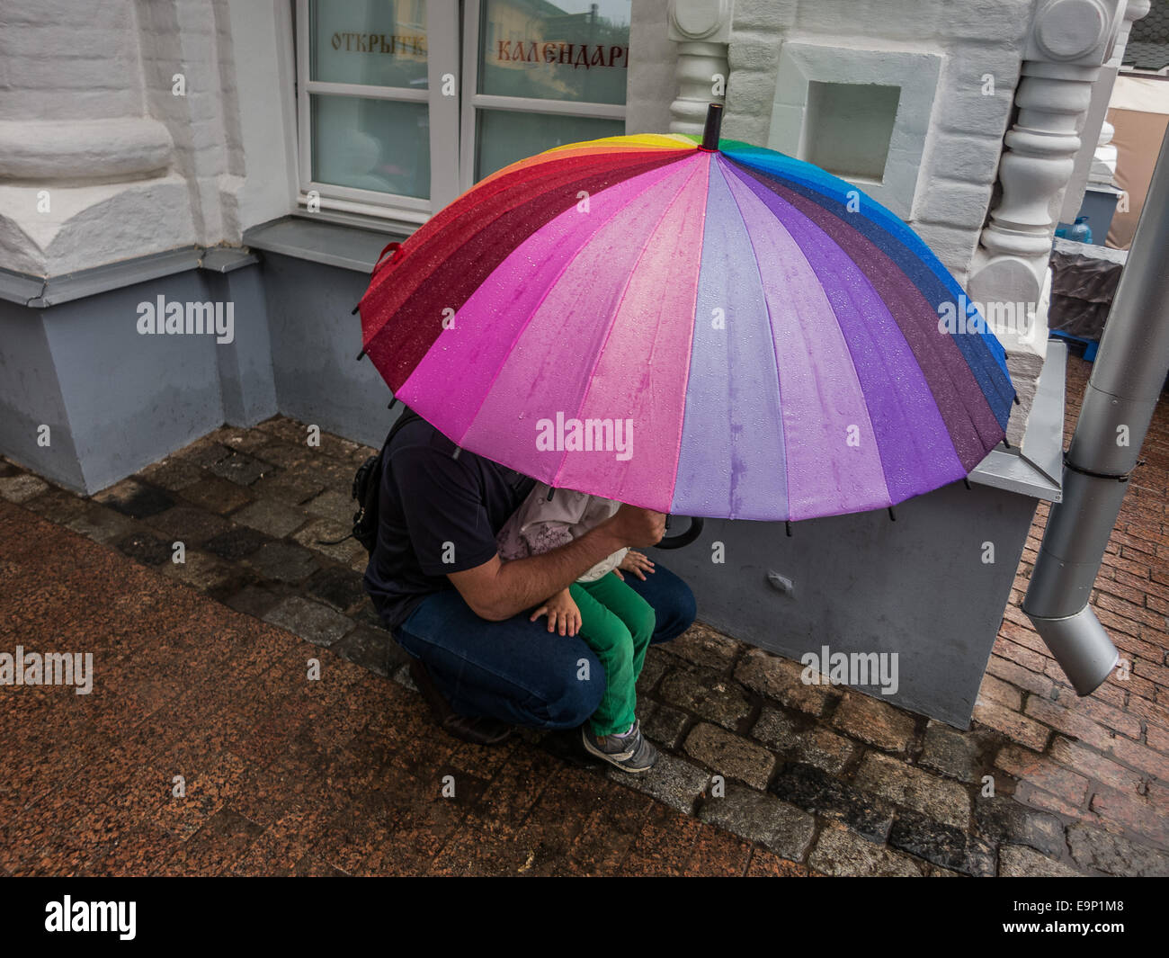 Father and child hiding from rain under colourful umbrella in Sergiev ...