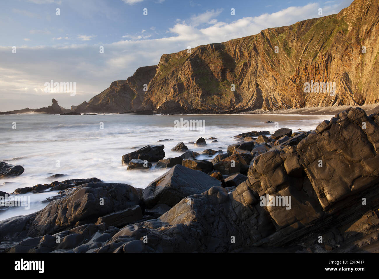 View of coastal cliff with folded strata in evening sunlight, Warren ...