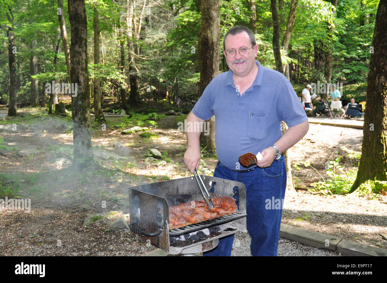 A middle-aged man cooks hamburgers and hotdogs, with lots of barbeque ...