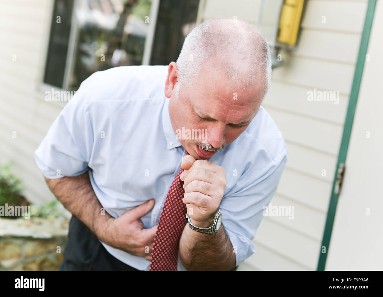 Mature businessman with gray hair, doubled over with a bad cough from a ...