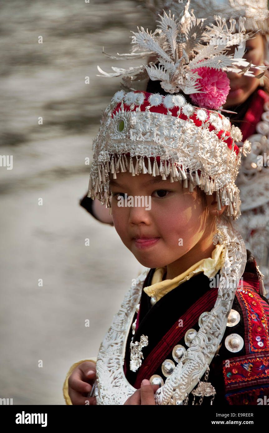 A young Miao girl with traditional wear and silver jewels in front of ...