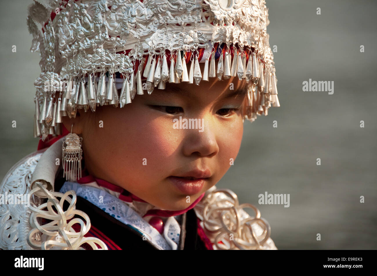 A young Miao girl with traditional wear and silver jewels in front of ...