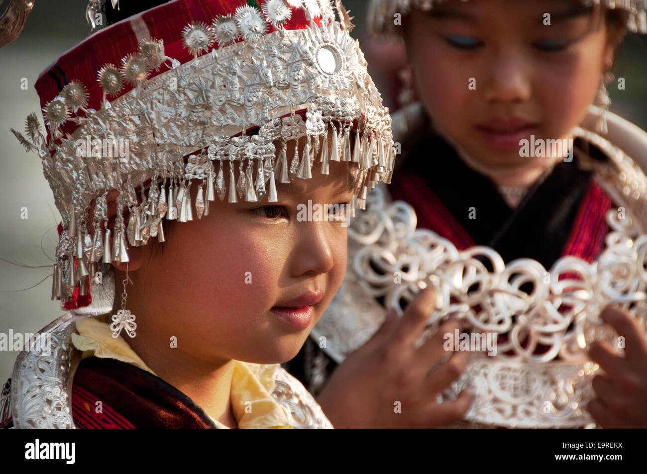 A young Miao girl with traditional wear and silver jewels in front of ...