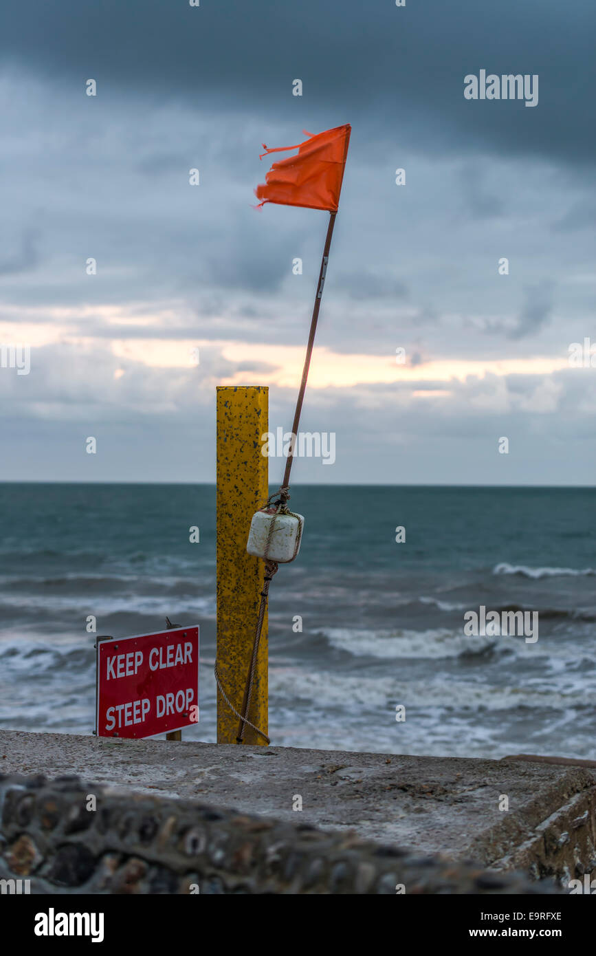Keep Clear Steep Drop warning sign on the beach next to an orange flag ...