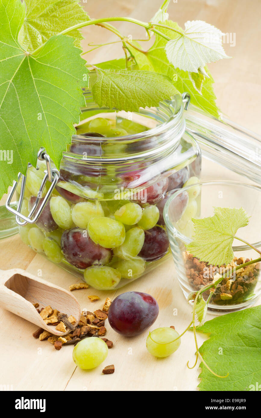 glass jar with canned grapes, grape leaves and spice on wooden table ...
