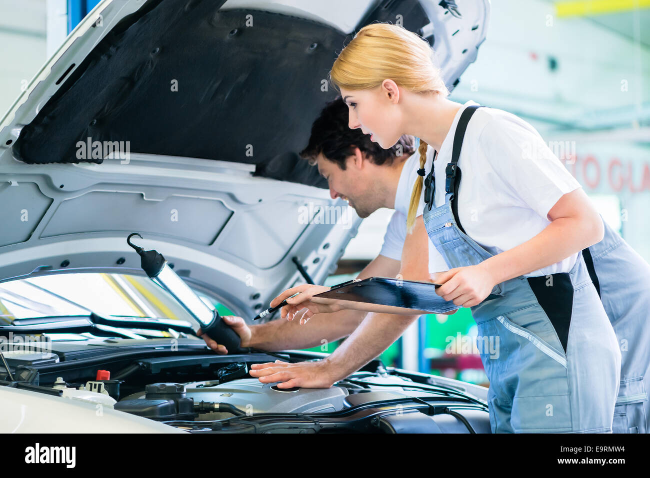 Male and female mechanic team examine car engine with light and ...
