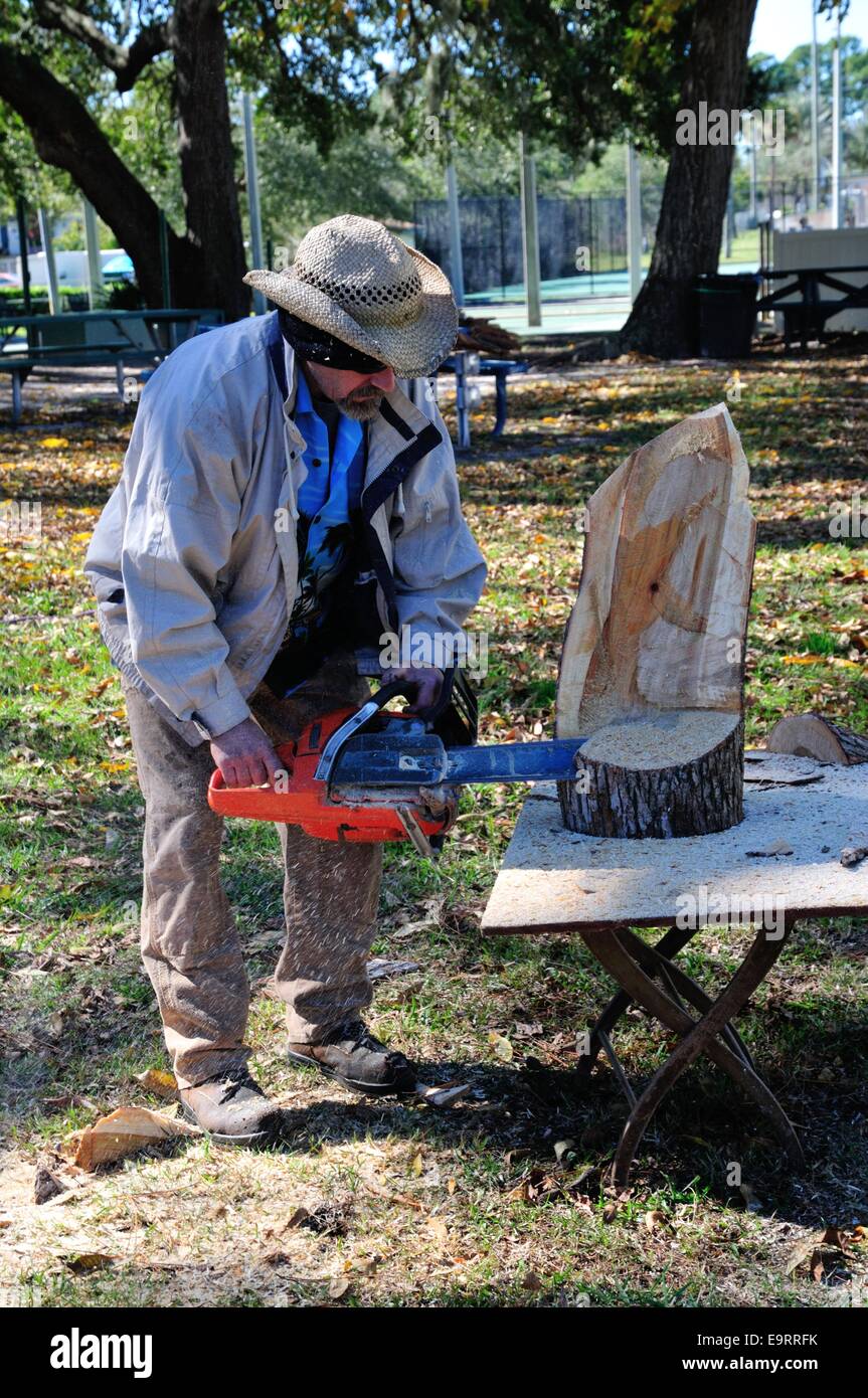 A chain saw sculptor sends wood chips flying as he works with part of a ...