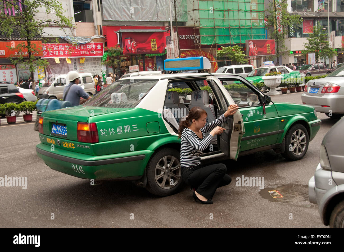 A lady taxi driver repairing a car door on the street, Kaili, China ...