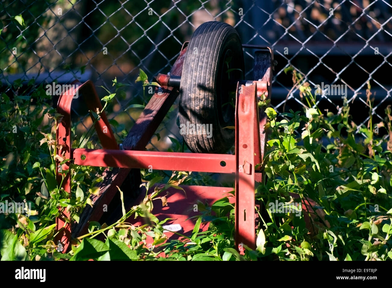 A red upside down wheel barrow in front of a metal chain fence laying ...