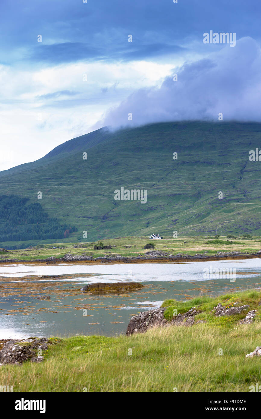 Small white solitary crofters cottage nestling below mountain range by ...